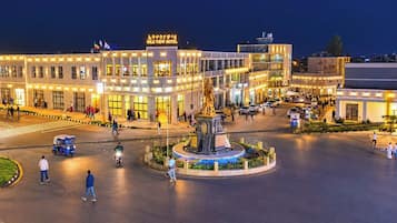 Hotel com um canteiro central, uma estátua e vários edifícios com placas iluminadas.