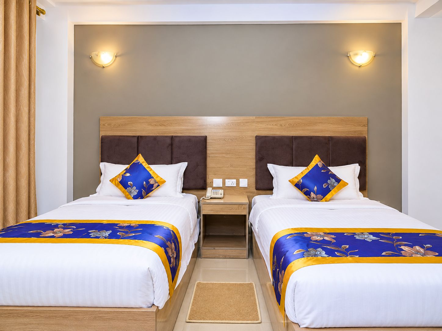 Quarto de hotel com duas camas, cada uma com cabeceira, mesa de cabeceira e luminária.