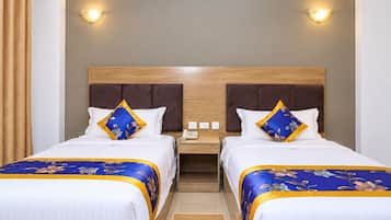 Quarto de hotel com duas camas, cada uma com cabeceira, mesa de cabeceira e luminária.