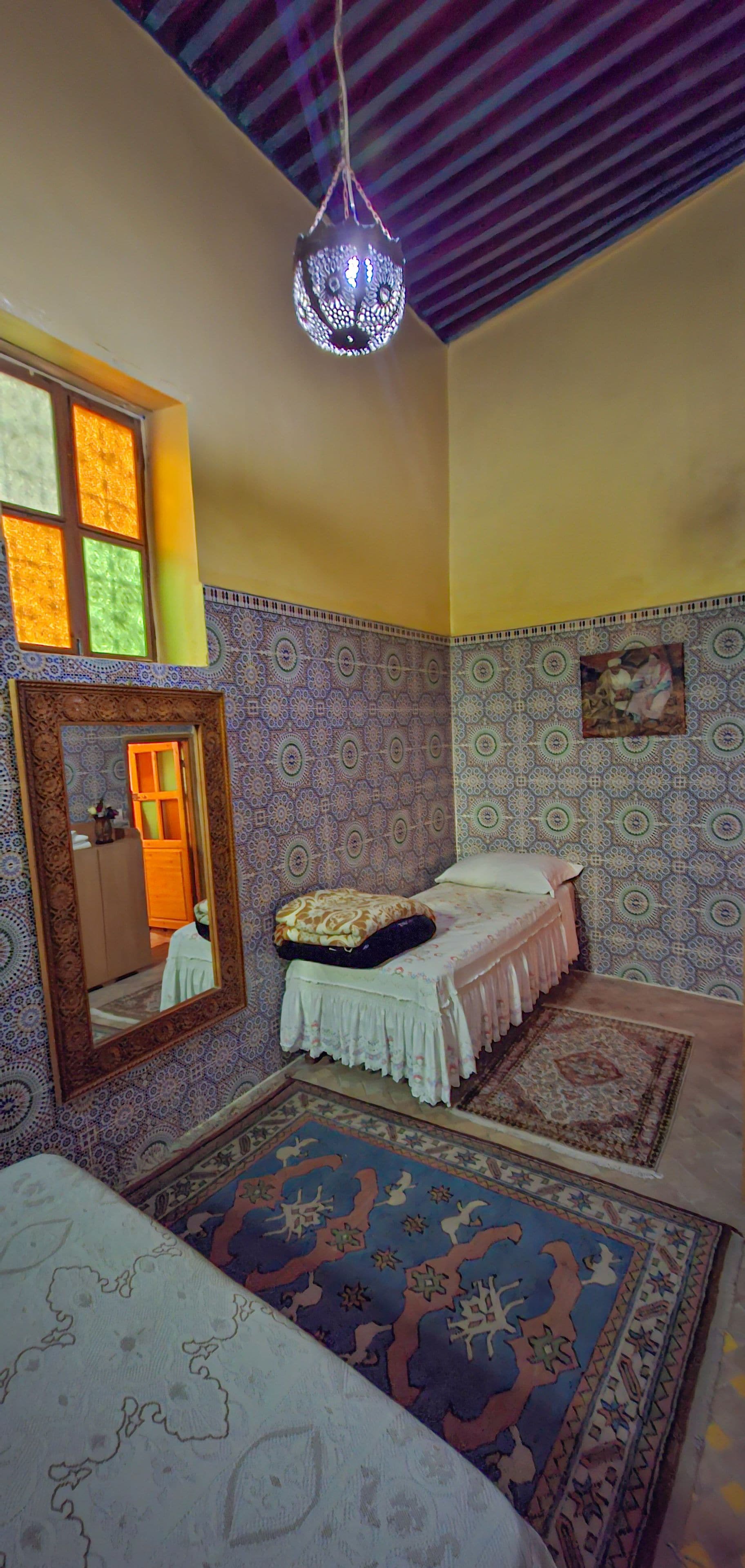 Quarto com cama, espelho, luminária pendente, paredes estampadas e tapete.