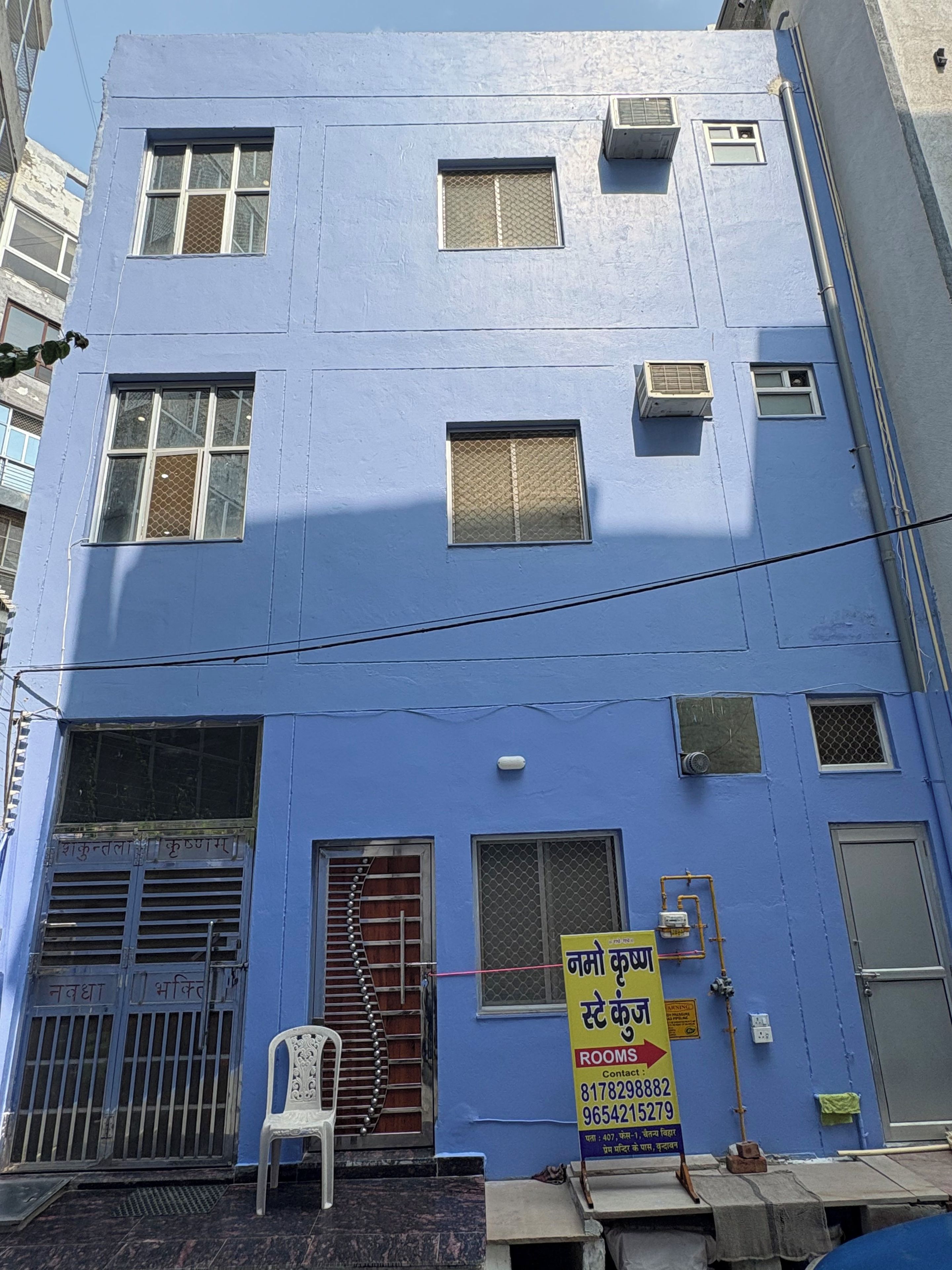 Edifício de vários andares com fachada azul, diversas janelas e uma placa anunciando quartos.