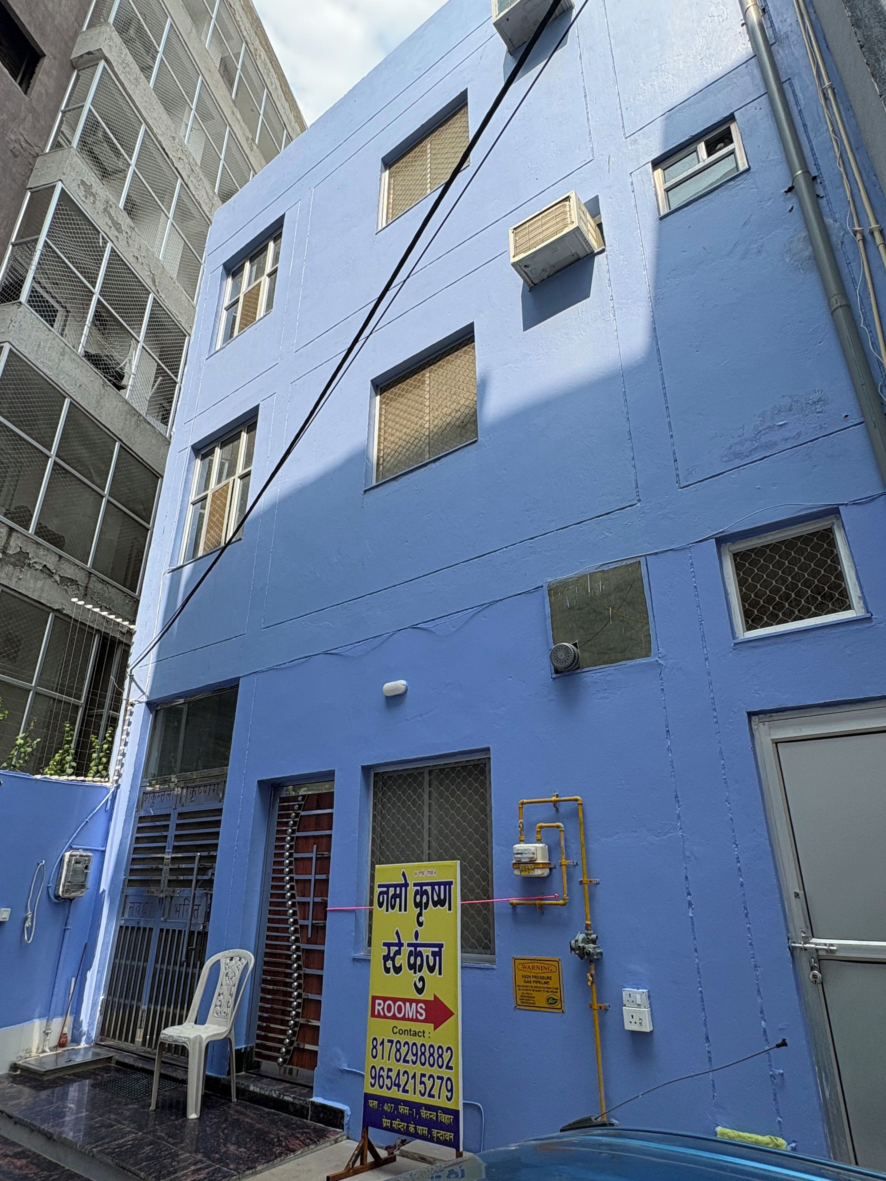 Um edifício de vários andares com fachada azul, diversas janelas e um aviso indicando quartos para alugar.