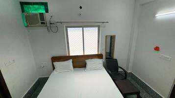 Quarto com cama, janela, ar-condicionado fixado na parede, mesa de cabeceira e cadeira.