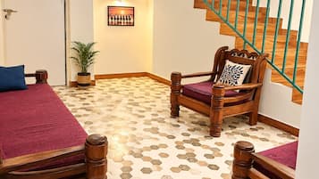 Quarto com cama de madeira, cadeira de madeira com almofada, planta em vaso e escada com degraus de madeira e corrimão verde.