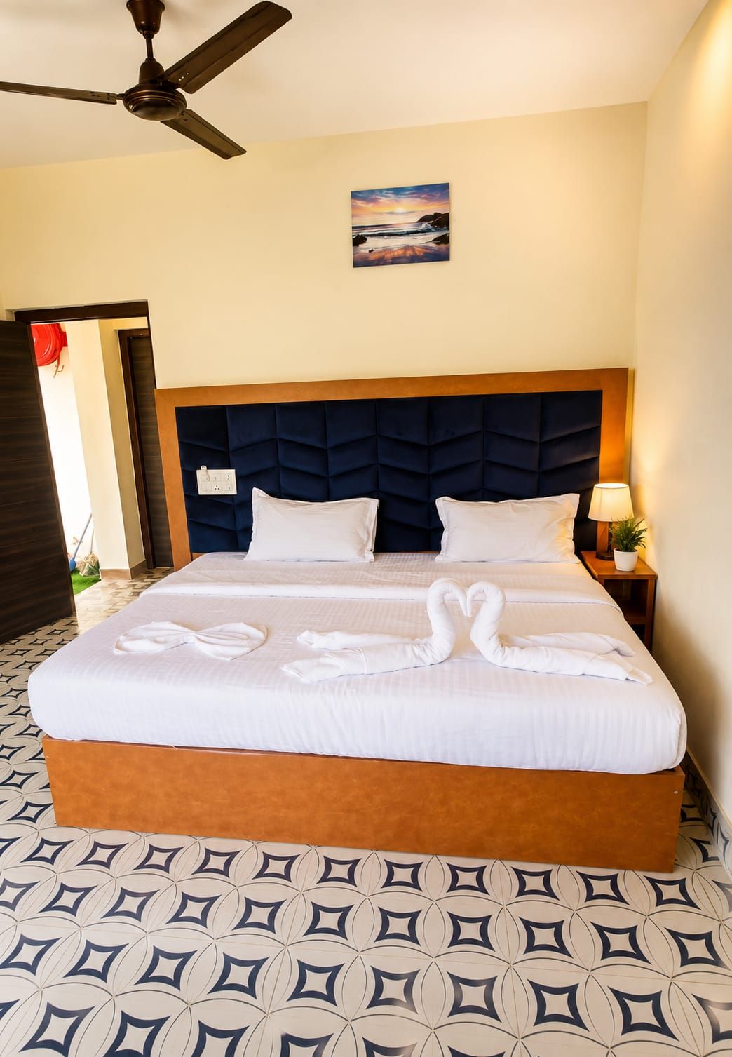 Quarto de hotel com cama, cabeceira, mesa de cabeceira, luminária e ventilador de teto.
