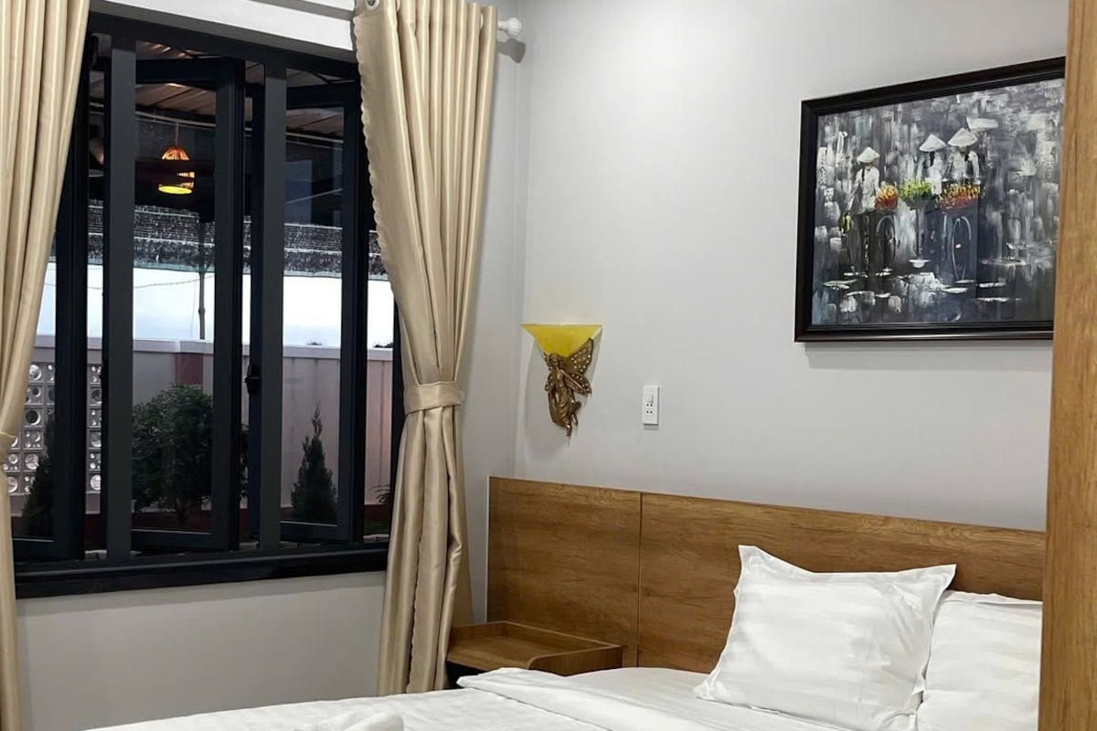 Quarto de hotel com cama, cortinas, luminária na parede e um quadro.