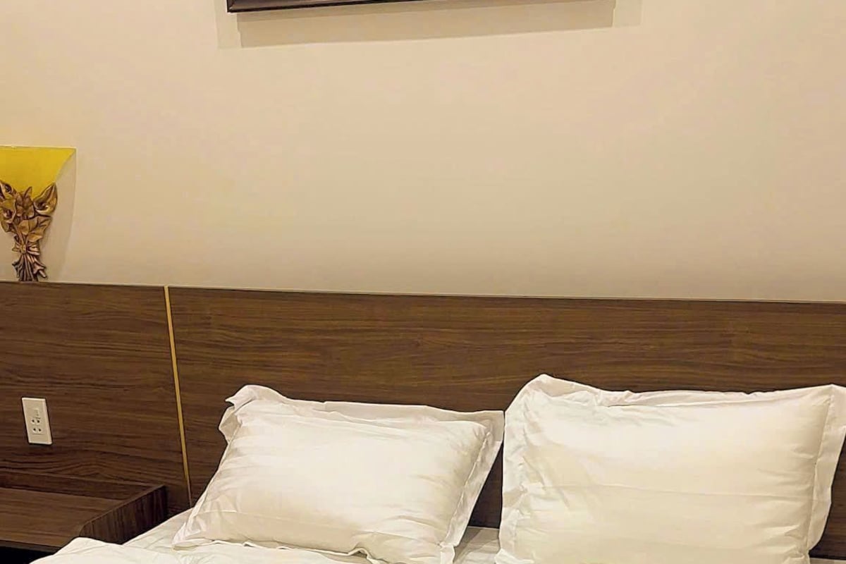 Cama bem arrumada com lençóis e almofadas brancos, toalha dobrada no apoio para os pés e um quadro acima da cama.