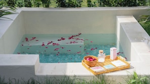 Piscina retangular com água e pétalas de rosa, rodeada por um muro branco.