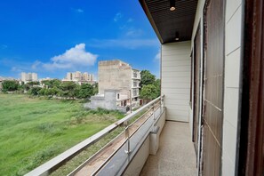 Uma varanda com vista para um campo gramado e edifícios ao longe.