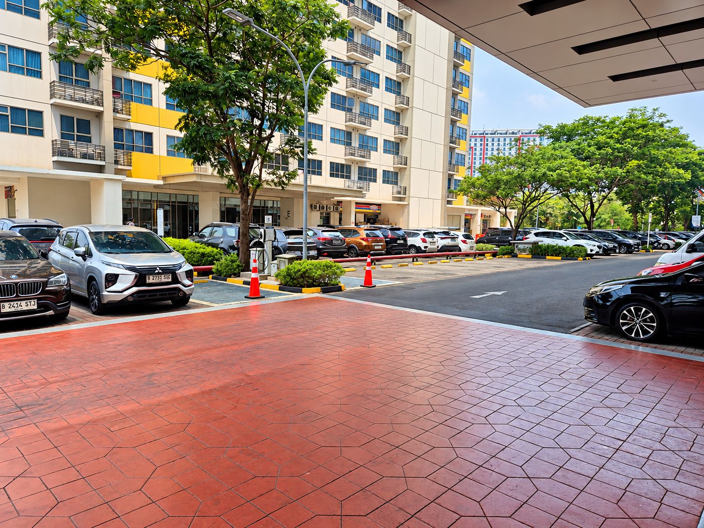 Uma área de estacionamento com vários carros, um edifício com varandas e uma árvore em primeiro plano.
