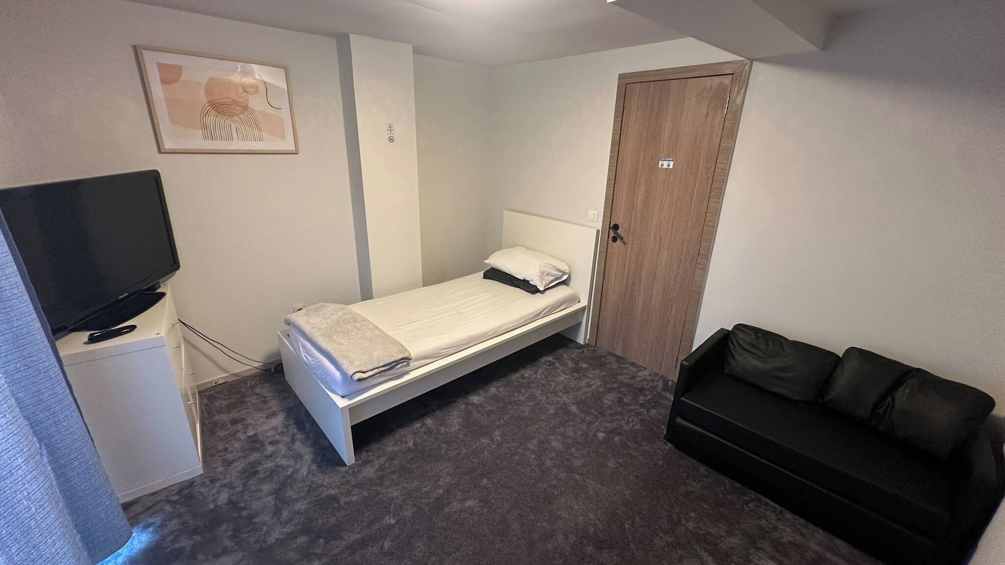 Quarto compacto com cama, televisão, guarda-roupa e sofá.