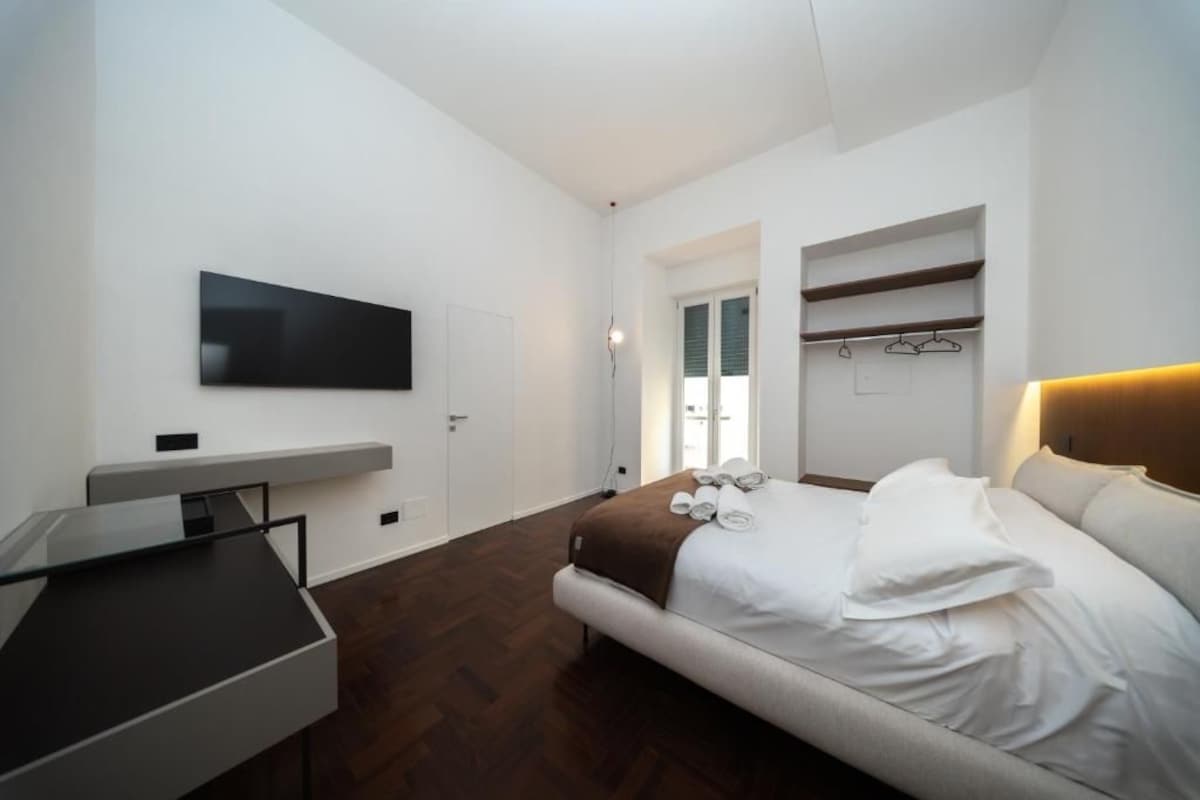 Quarto de hotel moderno com cama, TV de tela plana, escrivaninha e guarda-roupa.