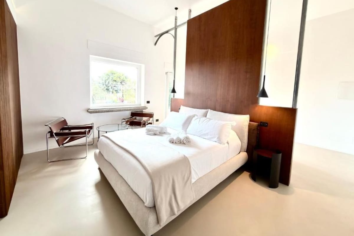 Quarto moderno com uma cama grande, mesa de cabeceira, uma cadeira e uma janela.