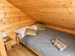 Um quarto pequeno e acolhedor, com uma cama de solteiro, uma mesinha de cabeceira e uma luminária.
