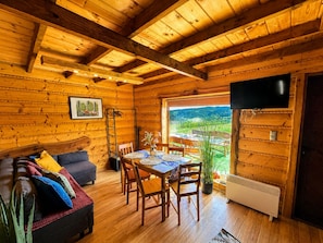 Interior acolhedor de uma cabana de madeira, com área de jantar, sofá e TV fixada na parede.