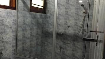 Casa de banho com chuveiro em cabine de vidro, paredes de mármore e um balde verde no chão.