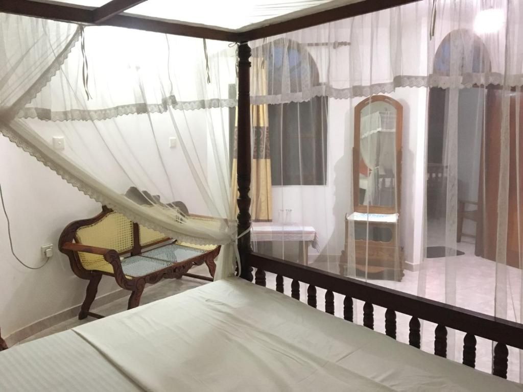 Quarto com cama, cadeira e janela com vista para um espelho e uma porta.