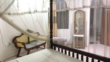 Quarto com cama, cadeira e janela com vista para um espelho e uma porta.