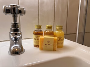 Uma pia de banheiro com uma torneira cromada e três frascos de shampoo e condicionador ELSY.