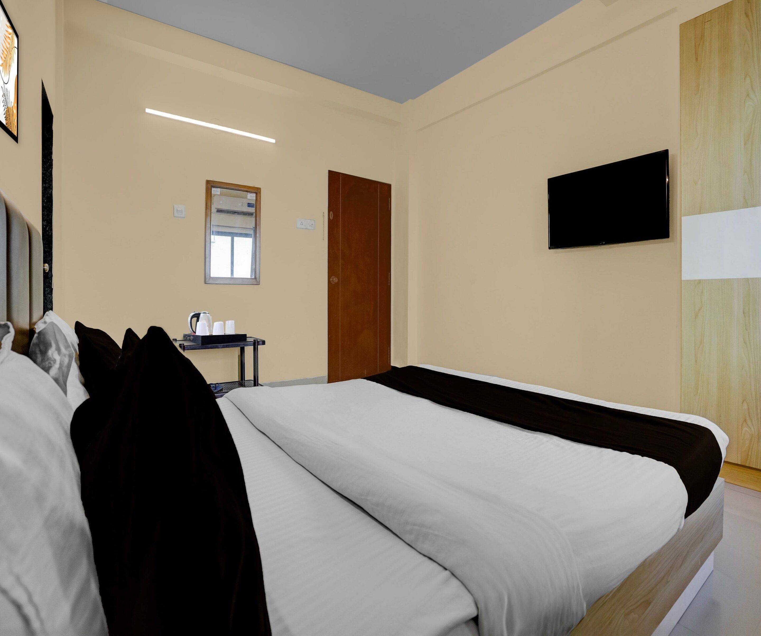 Quarto de hotel com cama, televisão de tela plana, mesa pequena com chaleira e janela.