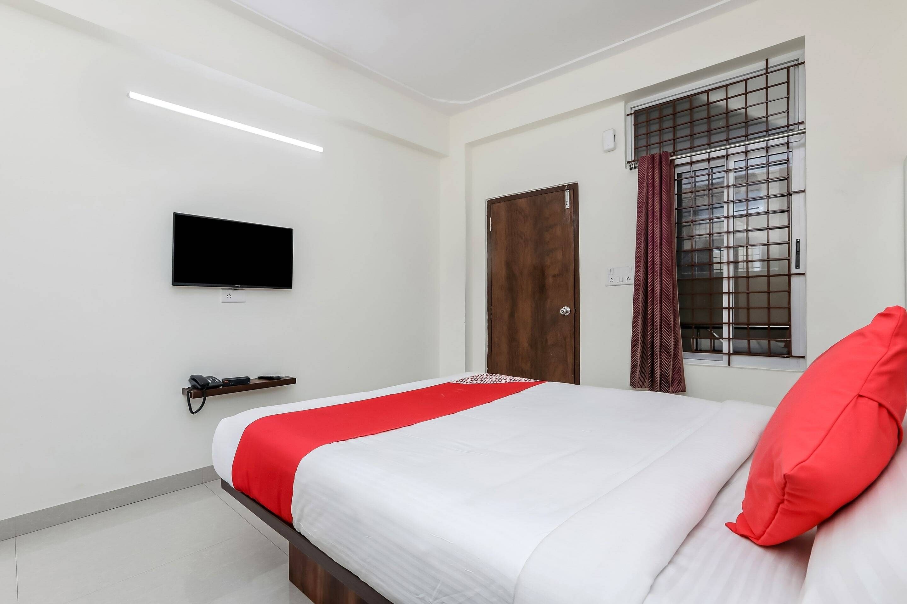 Quarto de hotel com cama, televisão presa à parede, janela com grades e porta.