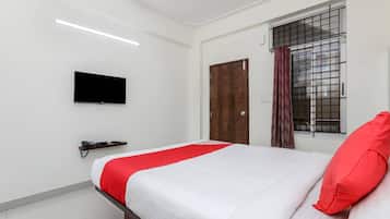 Quarto de hotel com cama, televisão presa à parede, janela com grades e porta.