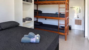 Quarto com beliche, guarda-roupa branco, banheiro pequeno e cama com colcha estampada.