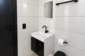 Casa de banho moderna com lavatório branco, armário preto e rolo de papel higiénico.