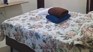 Um quarto com uma cama, televisão na parede e uma porta.