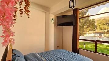 Quarto com cama, TV e janela com vista para o verde.