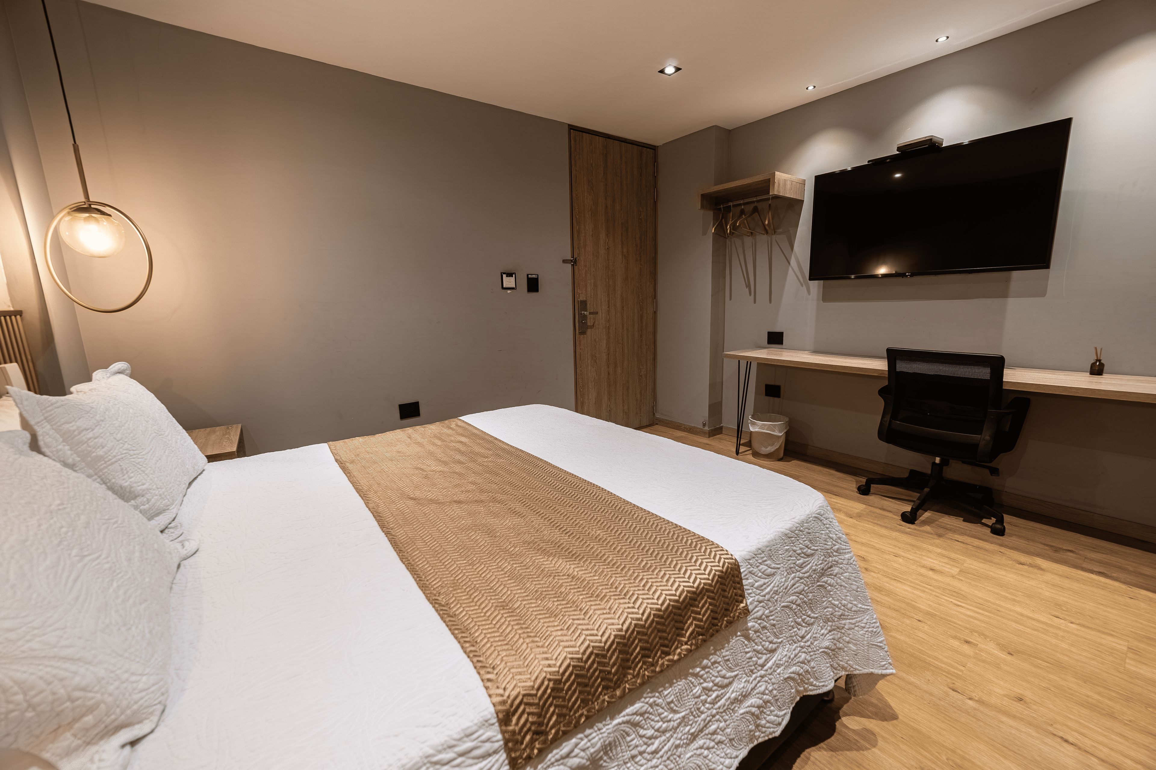 Quarto moderno com cama, escrivaninha, cadeira e televisão na parede.