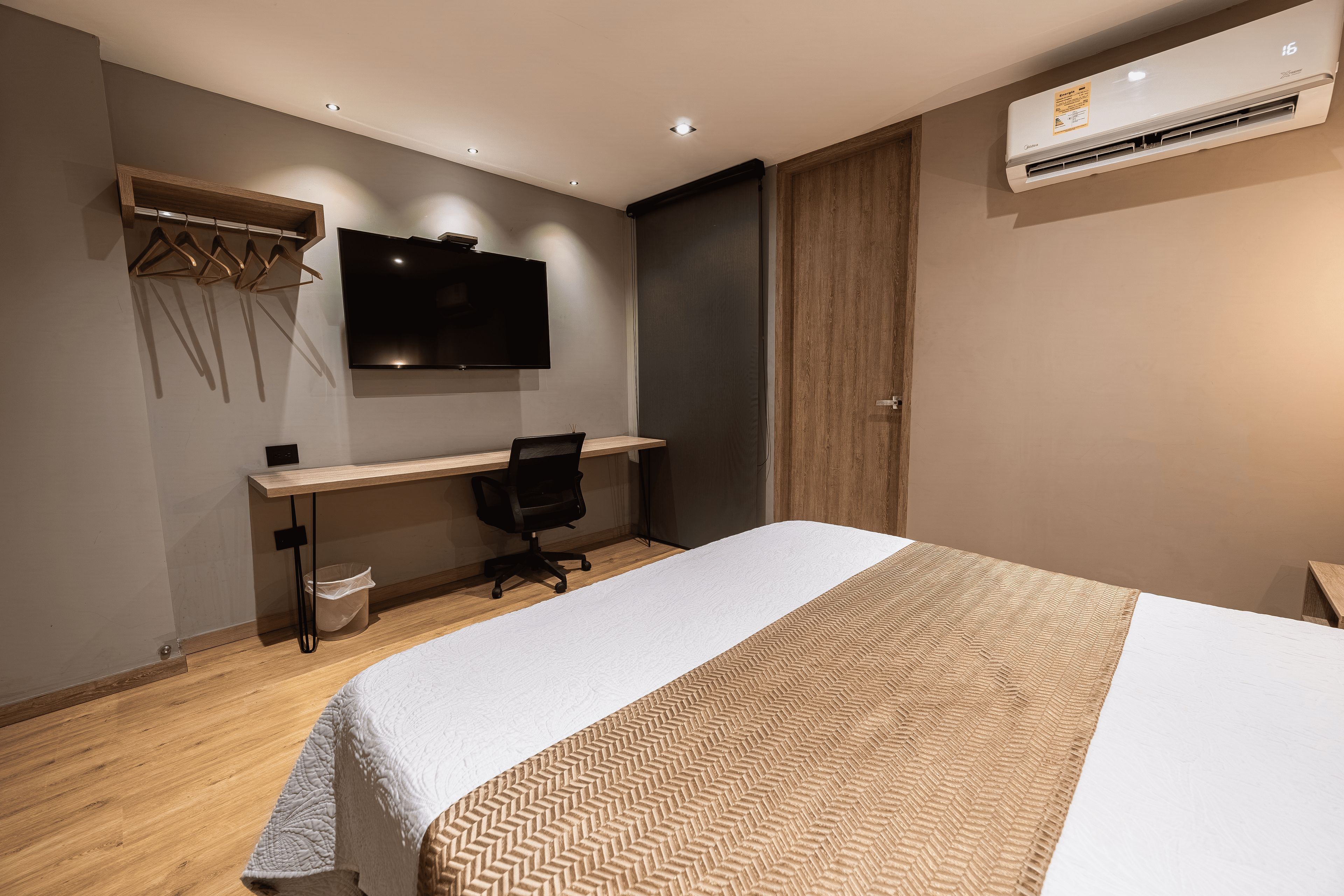 Quarto de hotel moderno com cama, escrivaninha, cadeira e televisão montada na parede.