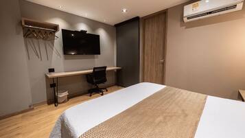 Quarto de hotel moderno com cama, escrivaninha, cadeira e televisão montada na parede.