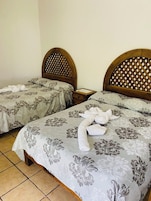 Quarto de hotel com duas camas, cada uma com cabeceira de madeira e colcha estampada com motivos florais.