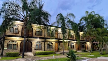 Um edifício de vários andares com fachada de pedra, janelas em arco e um gramado bem cuidado.