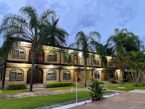 Um edifício de vários andares com fachada de pedra, janelas em arco e um gramado bem cuidado.