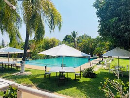 Piscina cercada por cadeiras, guarda-sóis e vegetação exuberante.
