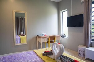 Quarto de hotel com cama, escrivaninha, cadeira, televisão e janela.