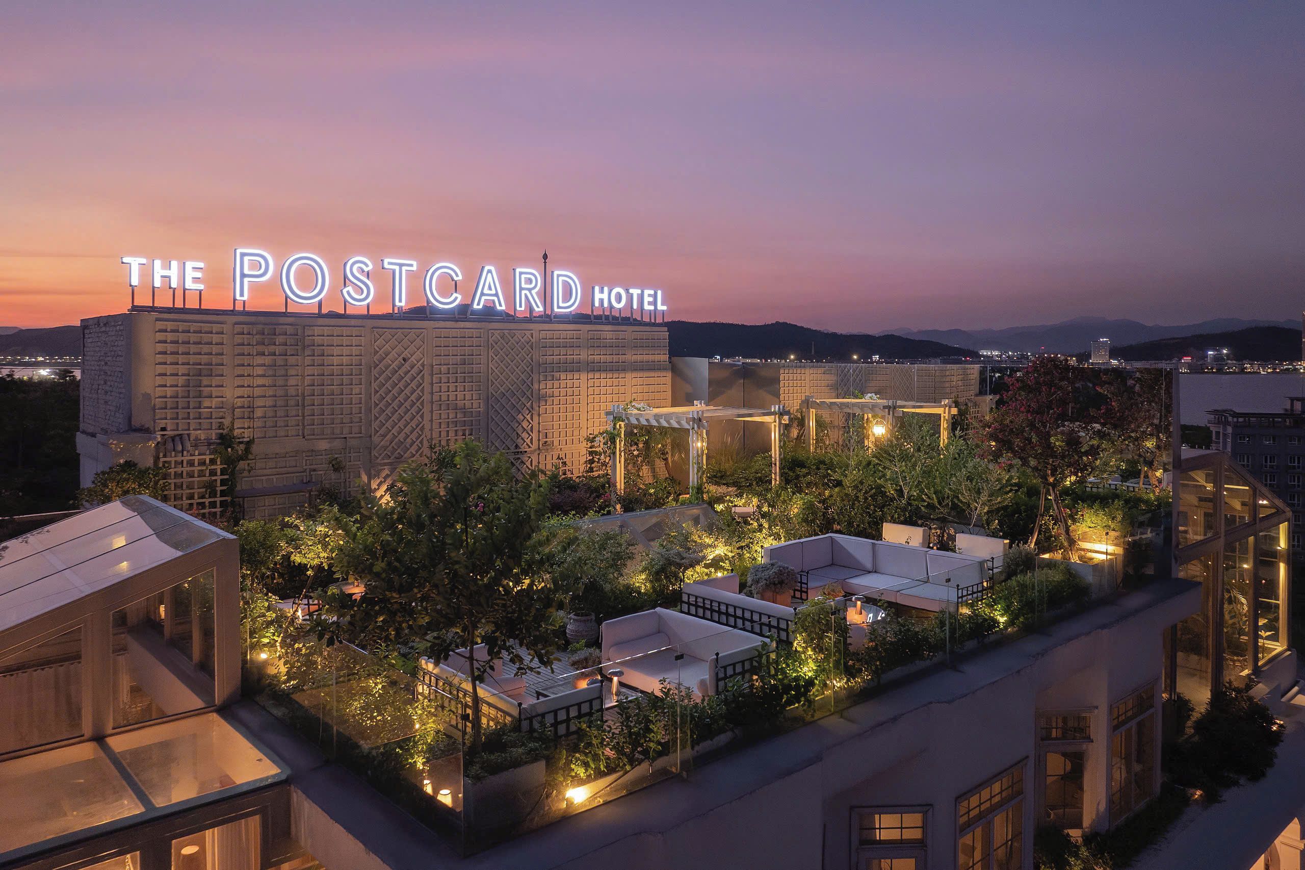 The Postcard Hotel com um jardim no terraço e um grande letreiro.