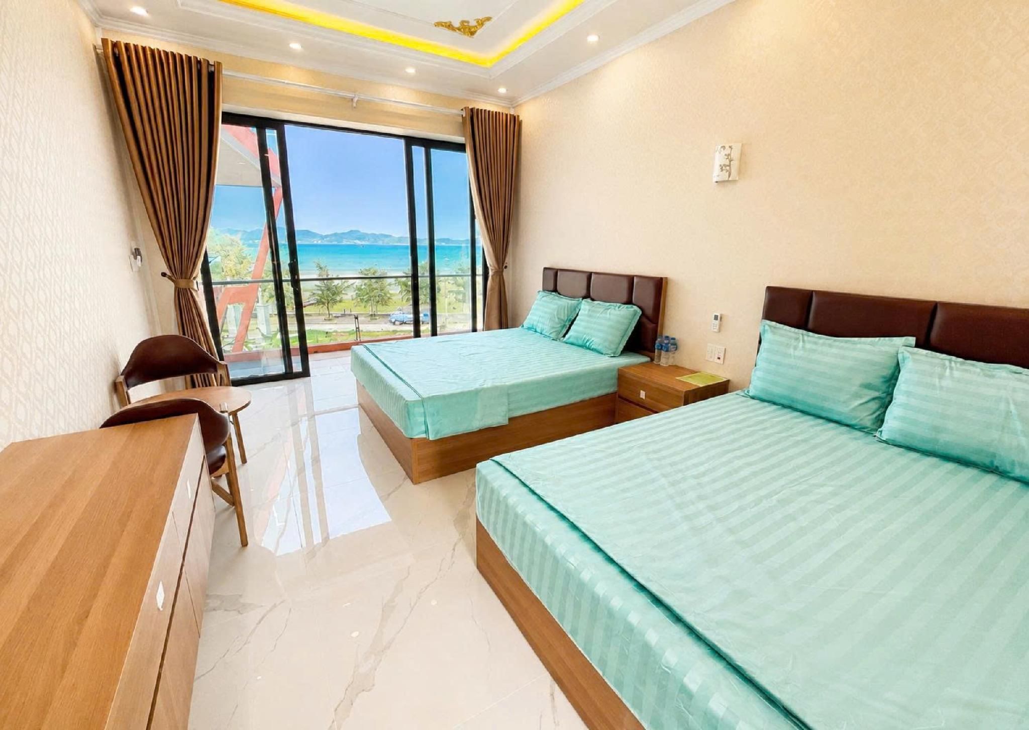 Quarto de hotel com duas camas, uma escrivaninha e vista para o mar.