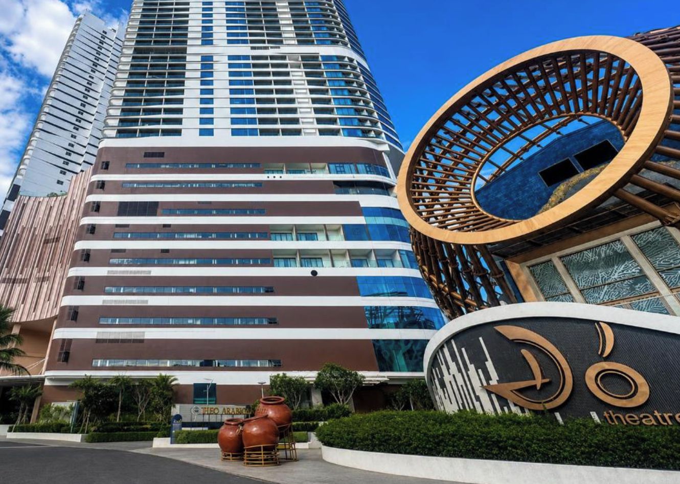 Hotel moderno com fachada curva, entrada circular destacada e placa visível de um teatro.