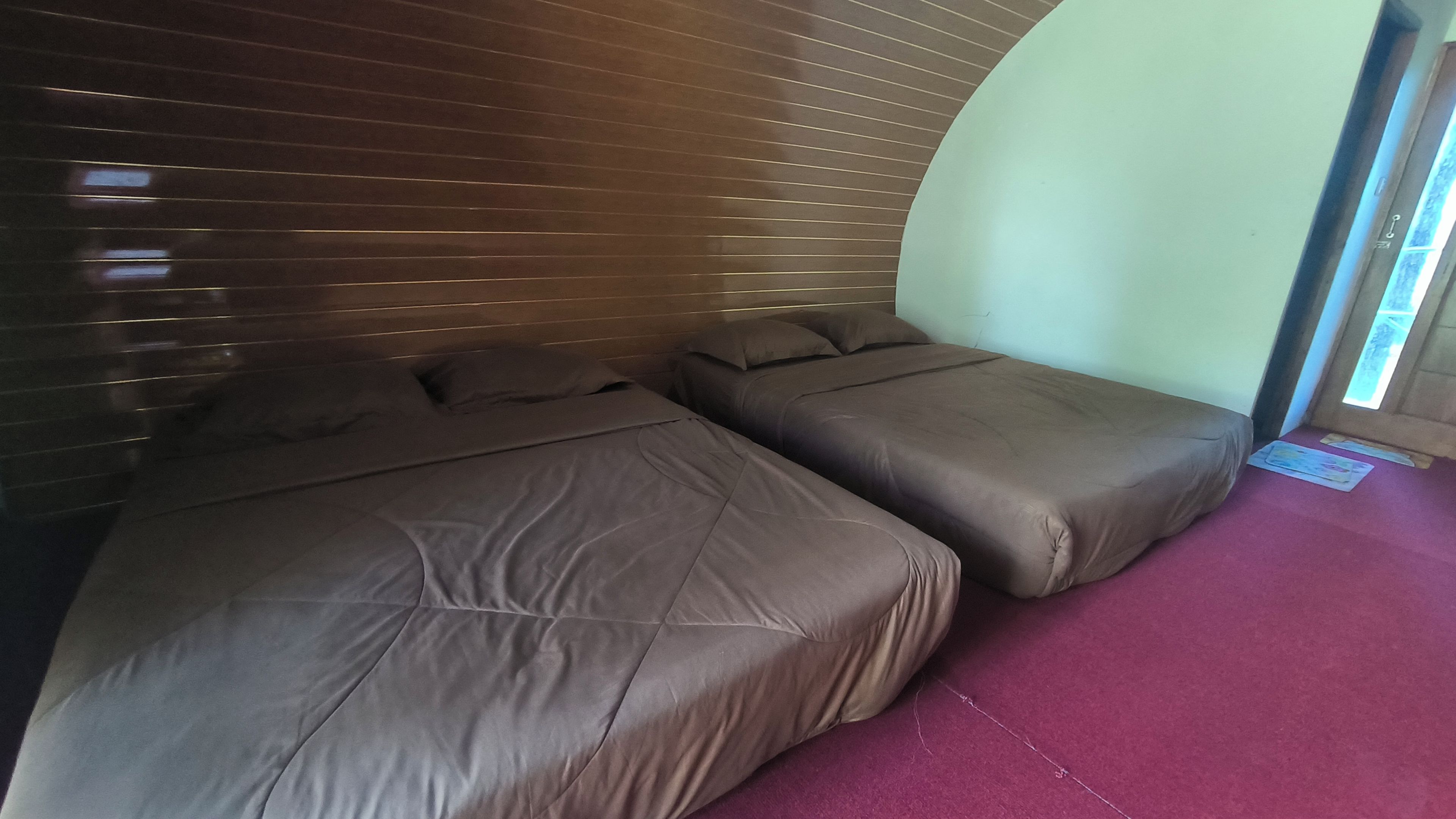 Quarto com duas camas, parede curva e porta para o exterior.