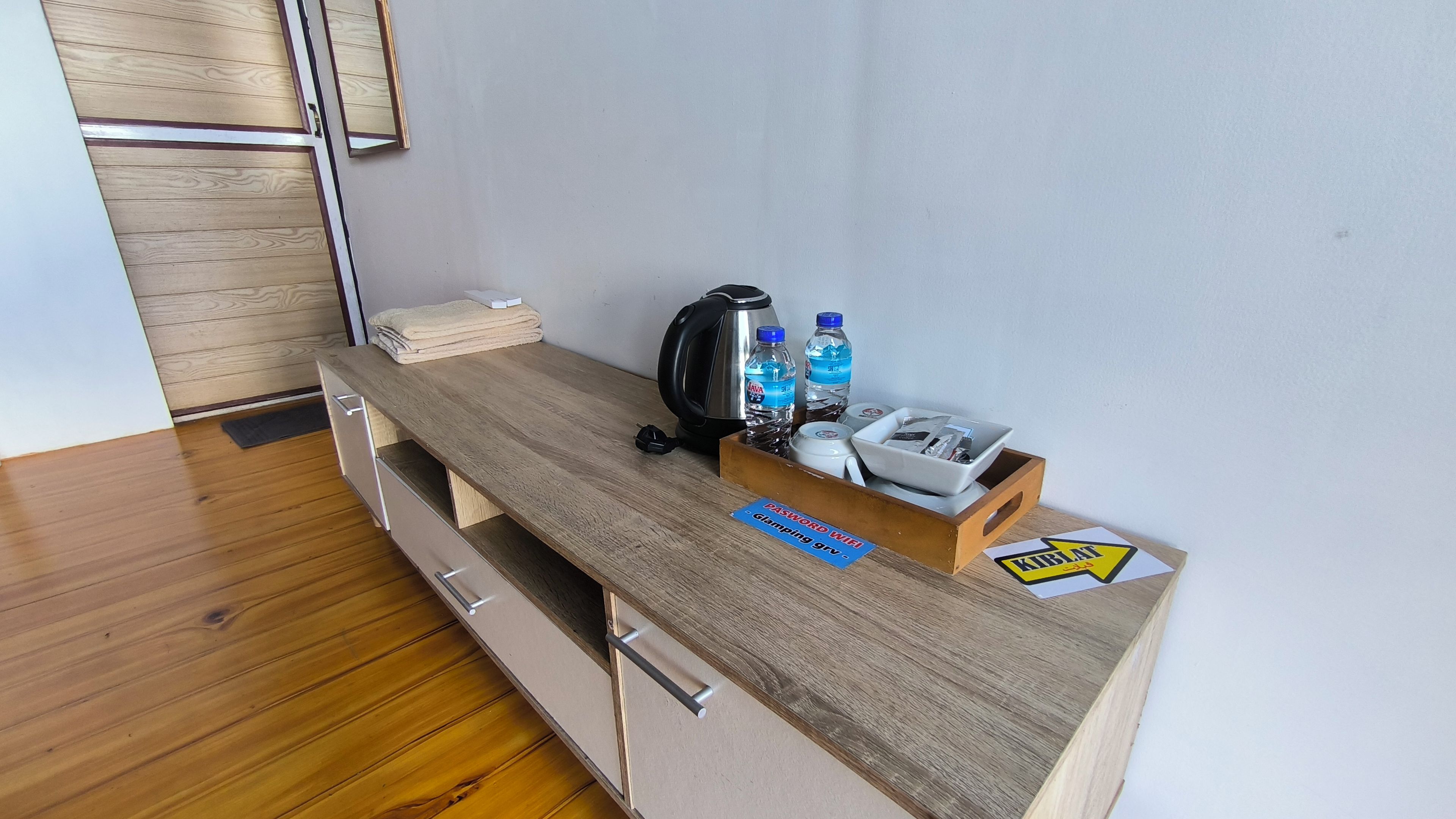 Uma cozinha compacta com bancada de madeira, chaleira, garrafas de água, cafeteira e aviso indicando disponibilidade de Wi-Fi.