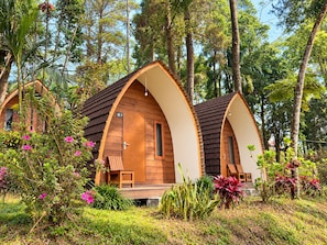 Uma fileira de cabanas de madeira com telhados inclinados, cercada por vegetação exuberante e plantas floridas.