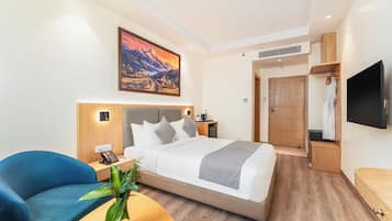 Quarto de hotel com cama, escrivaninha, cadeira, televisão e um quadro na parede.