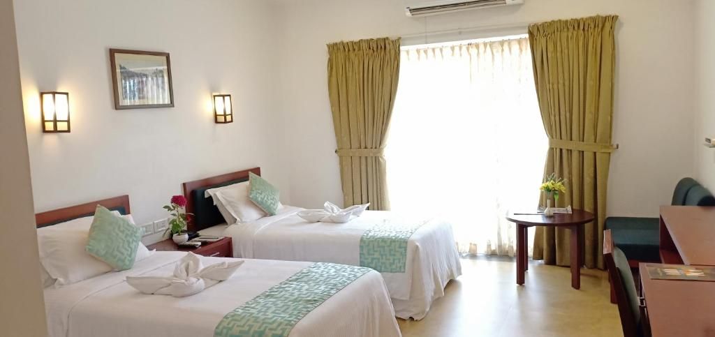 Quarto de hotel com duas camas, uma escrivaninha, uma cadeira e uma mesinha com um vaso de flores.