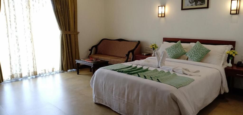 Quarto de hotel com cama, sofá, mesa de cabeceira e janela com cortinas.