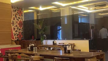 Interior de restaurante com mesas e cadeiras de madeira, um espelho grande e iluminação de teto moderna.