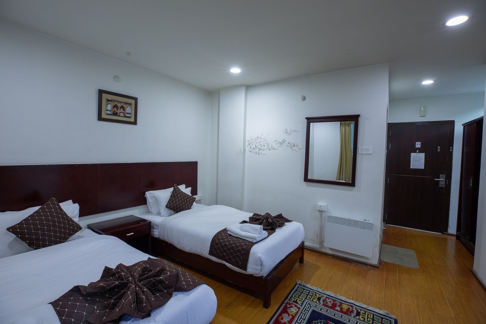 Quarto de hotel com duas camas, mesa de cabeceira, espelho, porta e radiador.