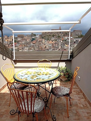 Terraço com mesa e cadeiras, com vista para uma cidade empoleirada em um morro.